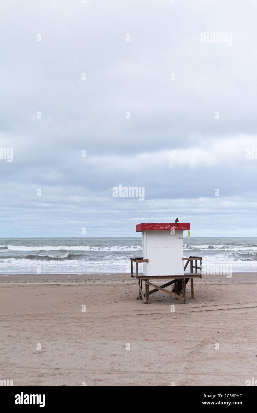 Small white cabin with red roof in the empty coast and the wavy sea ...