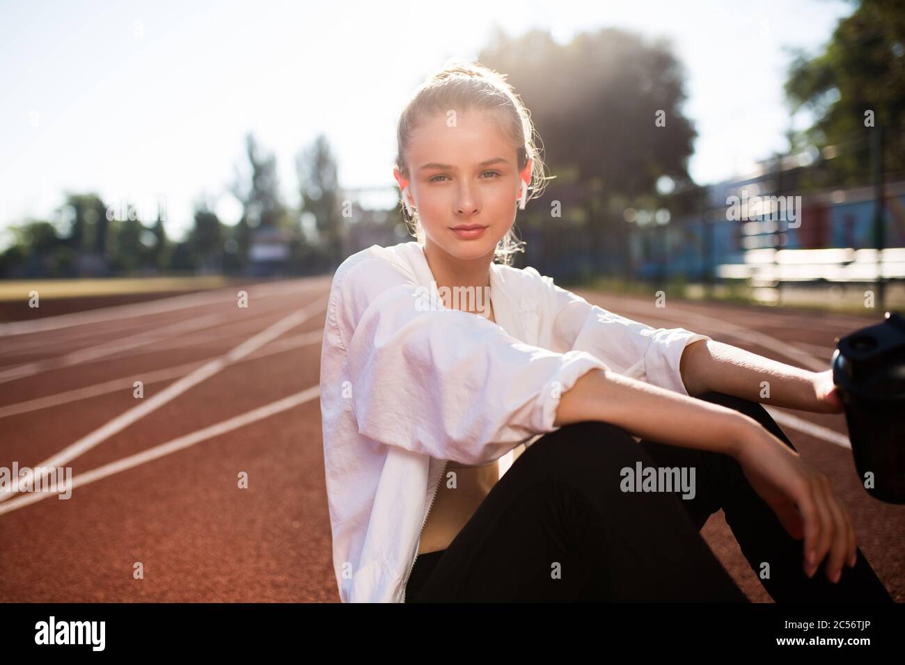 Beautiful sporty girl in wireless earphones dreamily looking in camera ...
