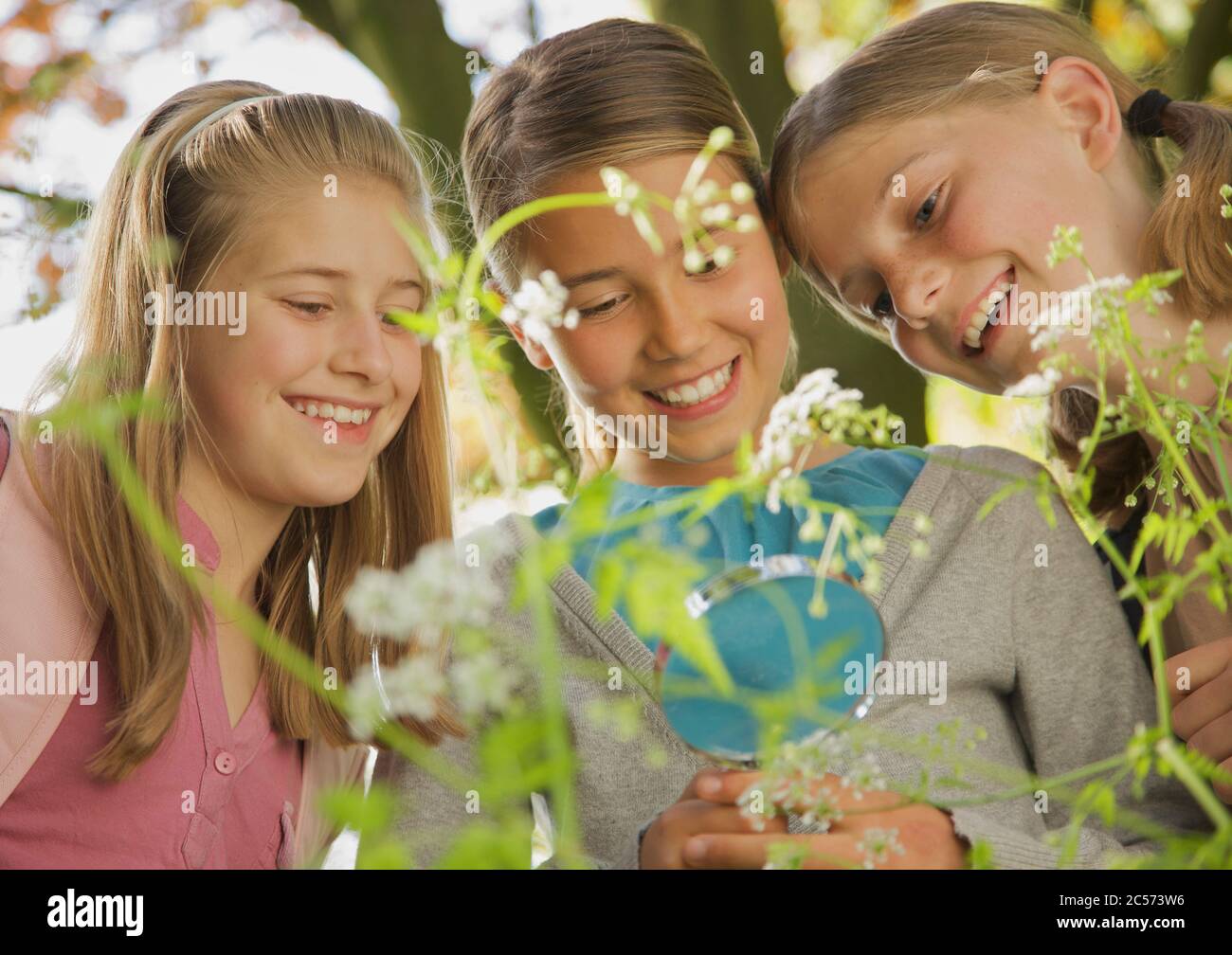 Smiling curious girls with magnifying glass examining flowers Stock ...