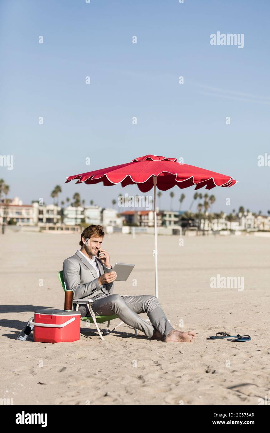 Barefoot businessman with smart phone and digital tablet working on ...