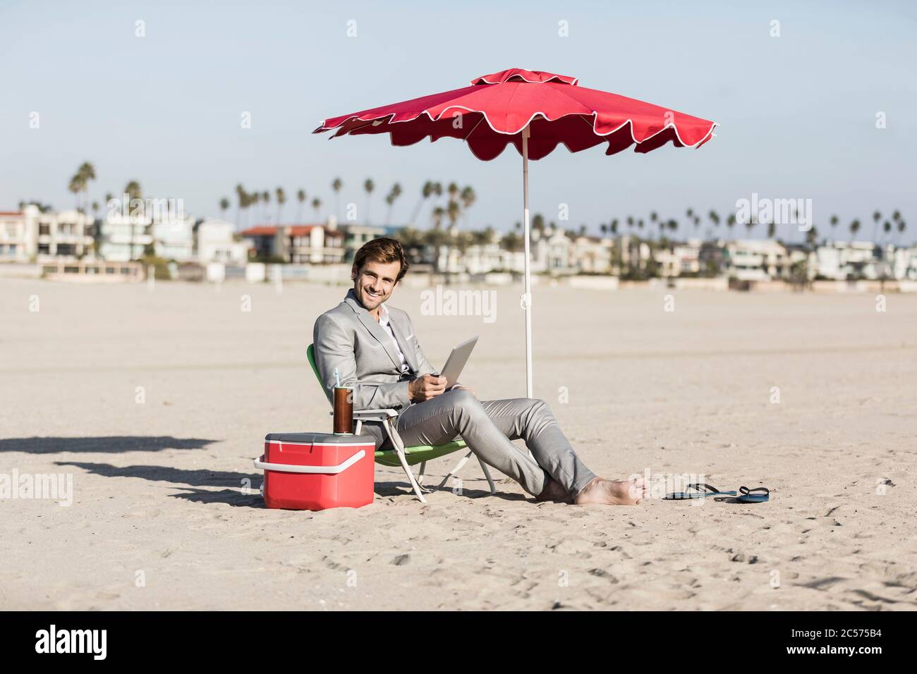 Portrait happy barefoot businessman working on sunny beach, Los Angeles ...