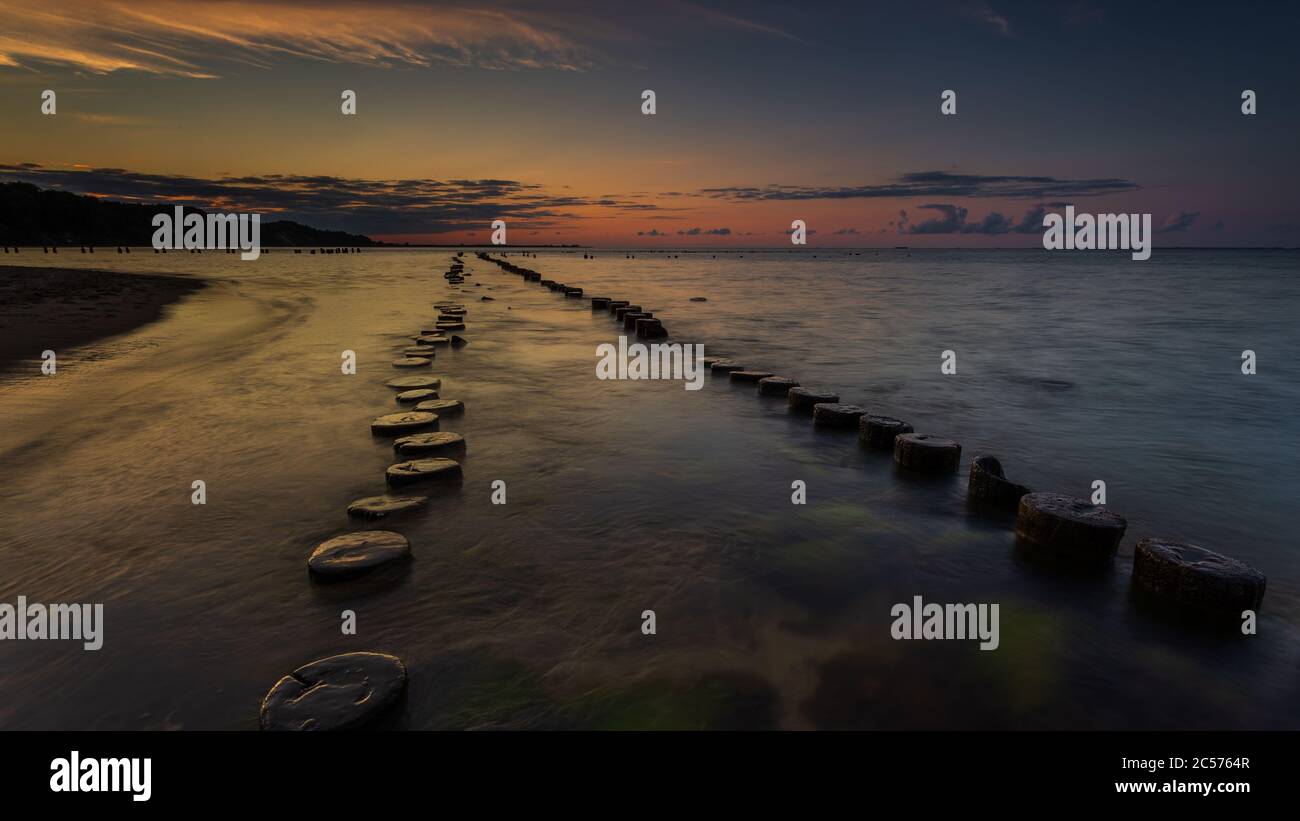 Sunset landscape at the sea. Wooden breakwaters line to the world war ...