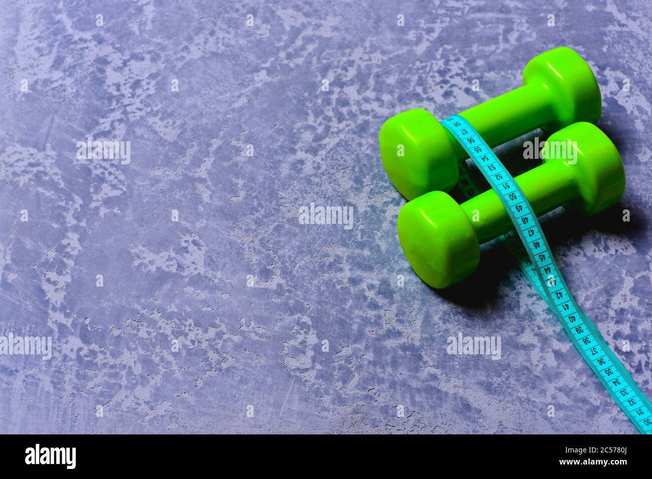 Dumbbells in green color and cyan measuring tape around them on grey ...