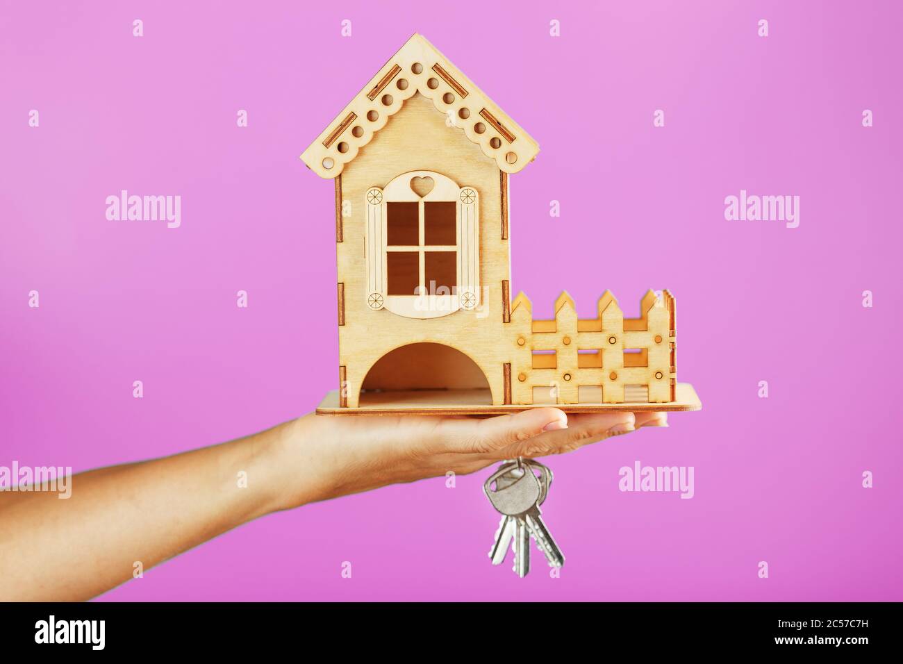 A small wooden house with keys in hand on a pink background Stock Photo ...