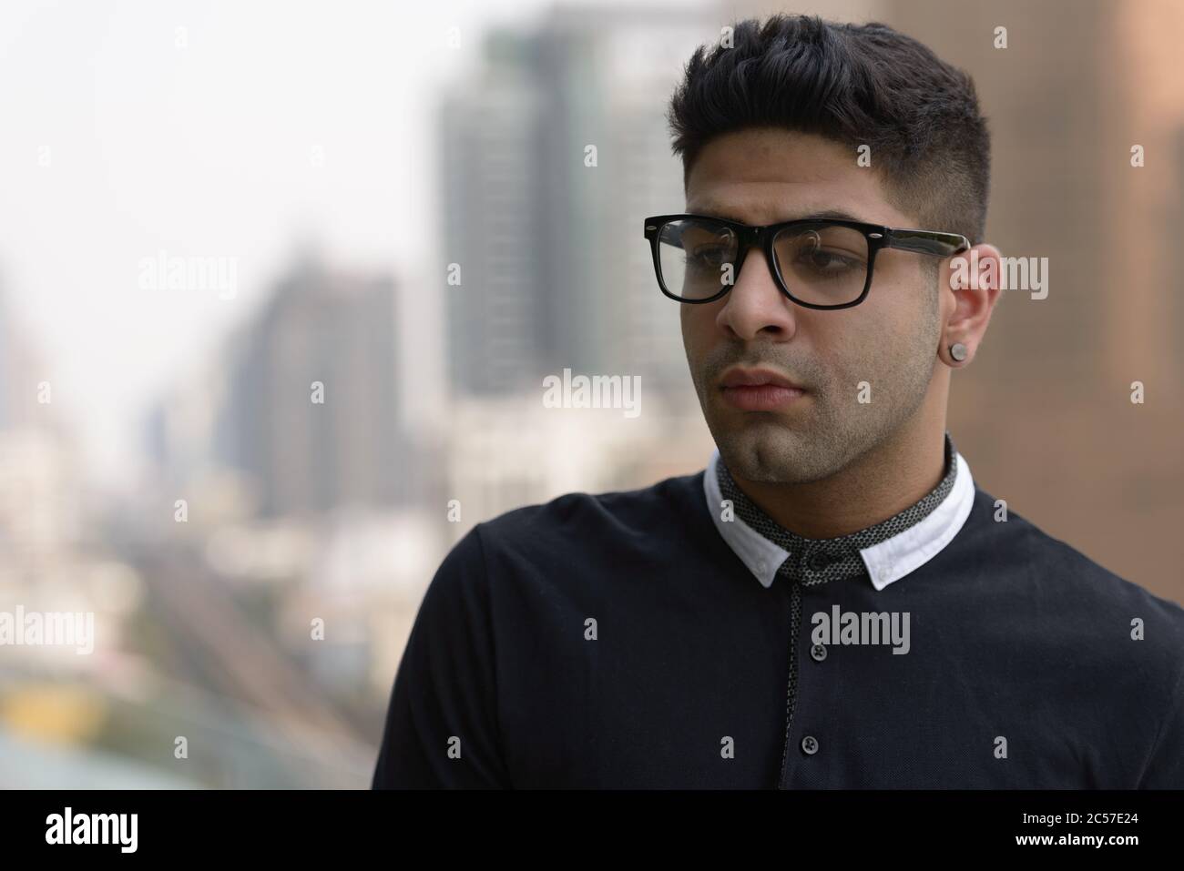 Face of stressed young Indian man with eyeglasses thinking in the city ...
