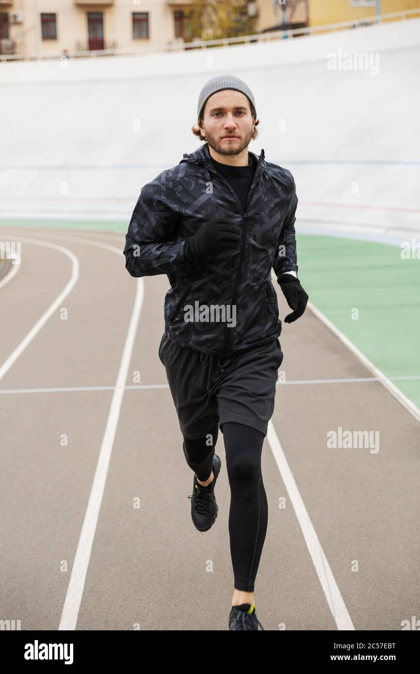 Confident young fit sportsman running on the race track at the stadium ...