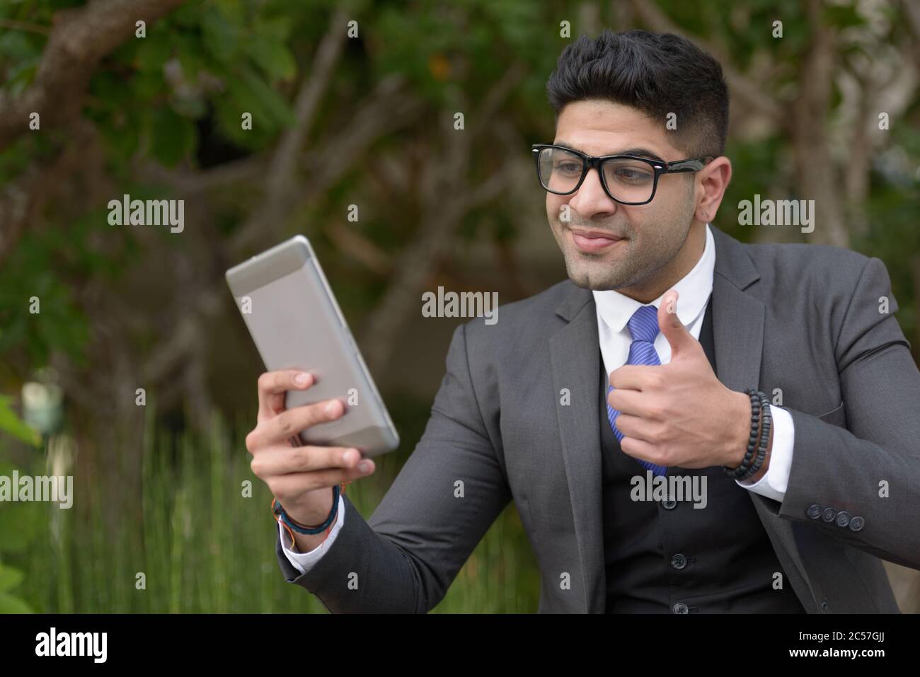 Young handsome Indian businessman with eyeglasses video calling with ...