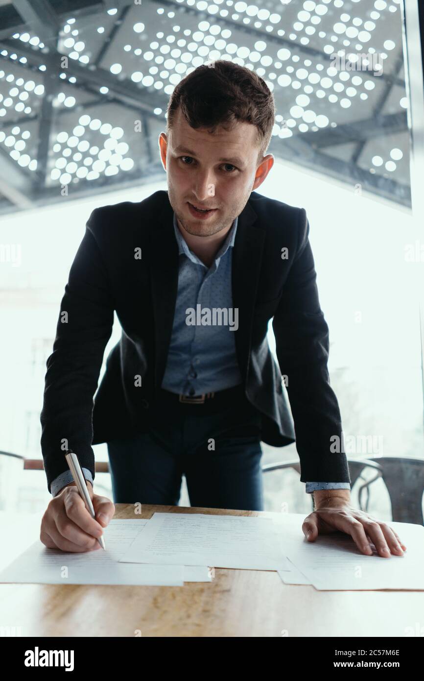 Confident young business man signing documents in a modern office with ...