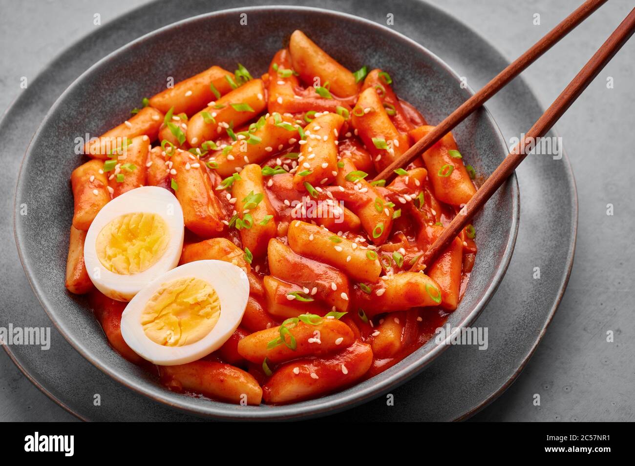 Tteokbokki with eggs in gray bowl on concrete table top. Tteok-bokki is ...