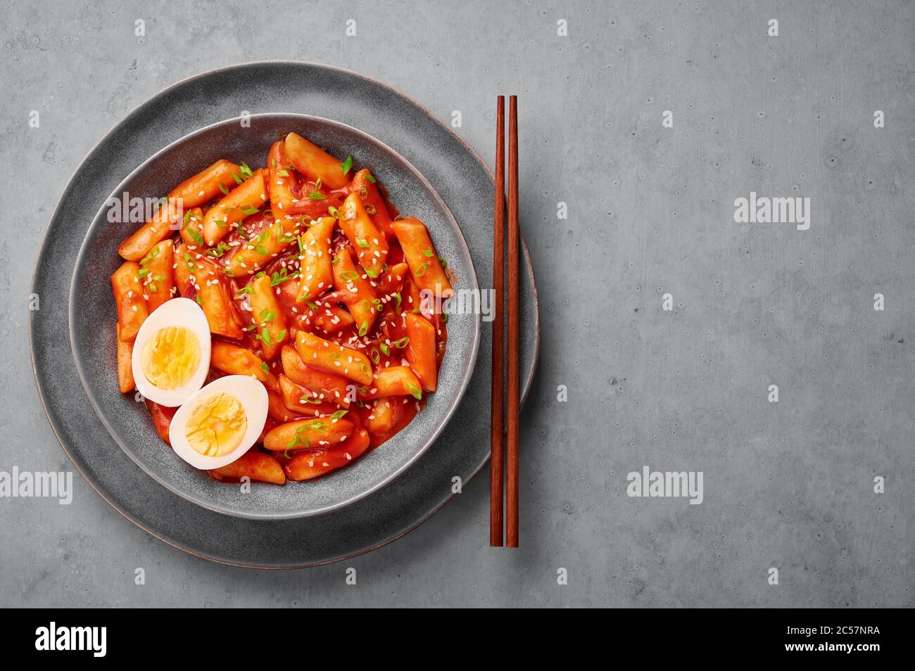 Tteokbokki with eggs in gray bowl on concrete table top. Tteok-bokki is ...