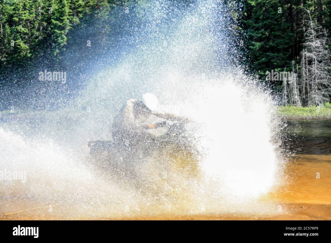 Man driving motocross ATV quad through splashing river lake water with ...