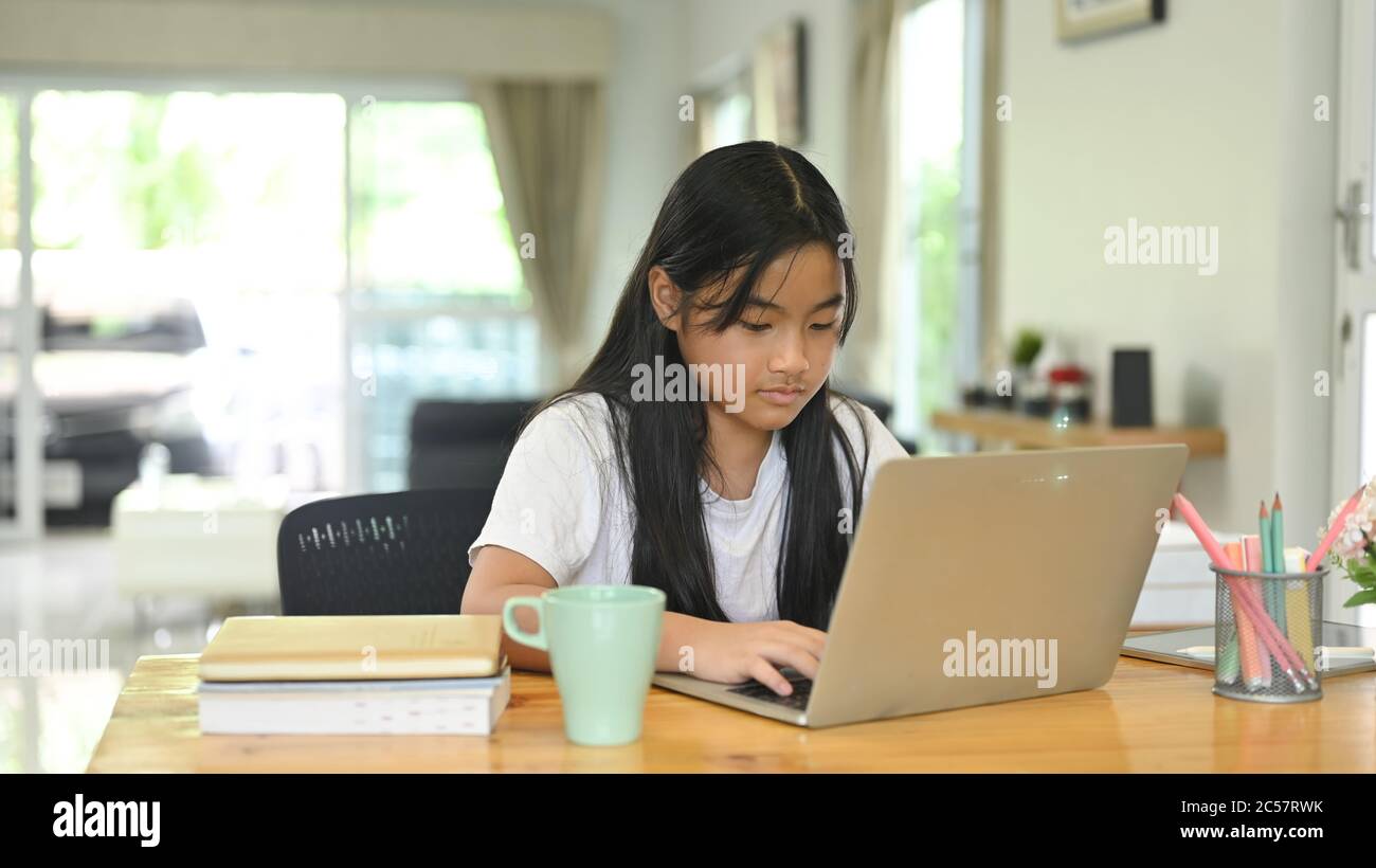 A school kid is doing her homework with a computer laptop at the wooden ...
