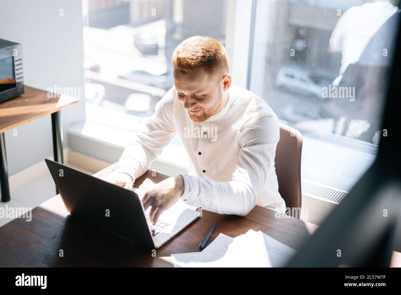 Smiling young business man using computer sitting at home office desk ...