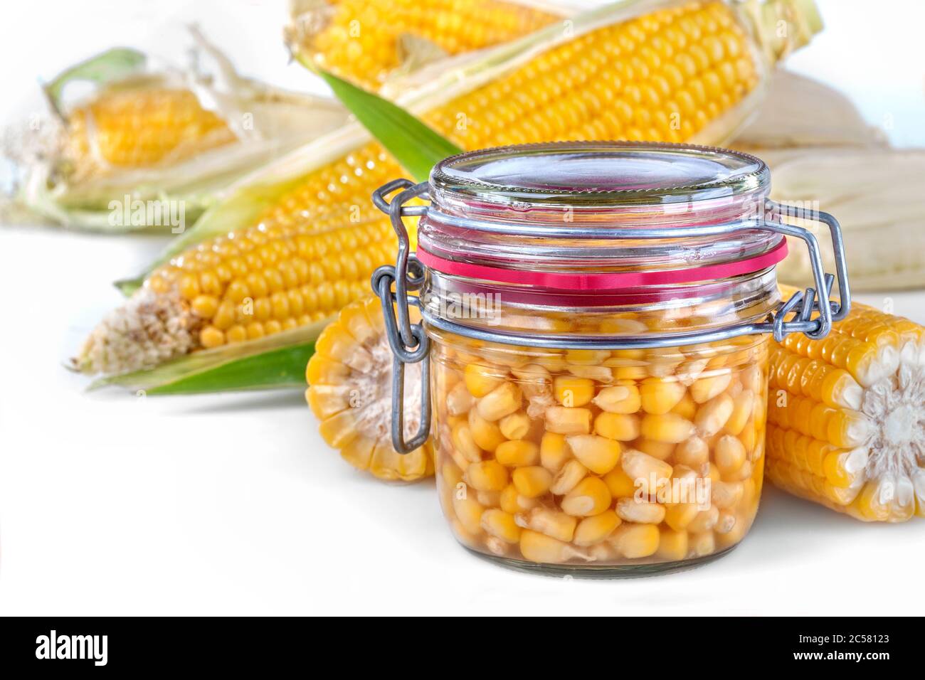 A glass jar filled with sweet canned corn. Fresh and cooked corn on ...