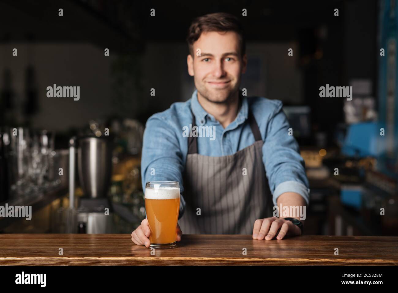 Celebrate in pub. Handsome guy gives glass of light beer with foam for ...