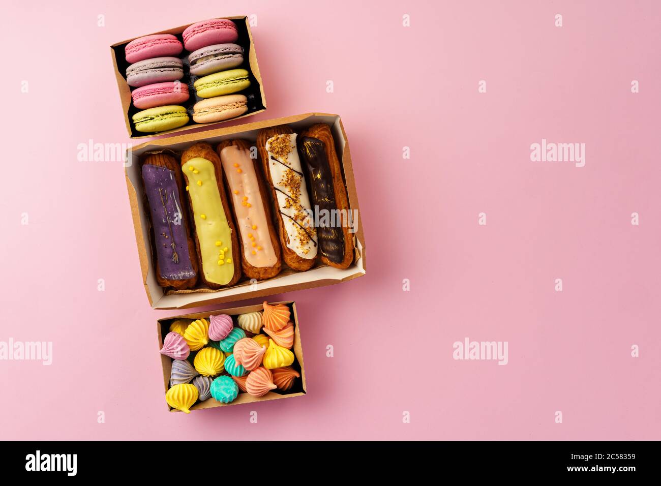 Carton boxes with eclair cakes and cookies on pink surface Stock Photo ...