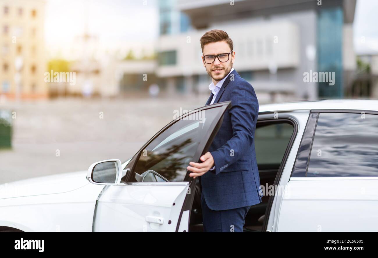 Confident young businessman getting into his car in downtown city area ...
