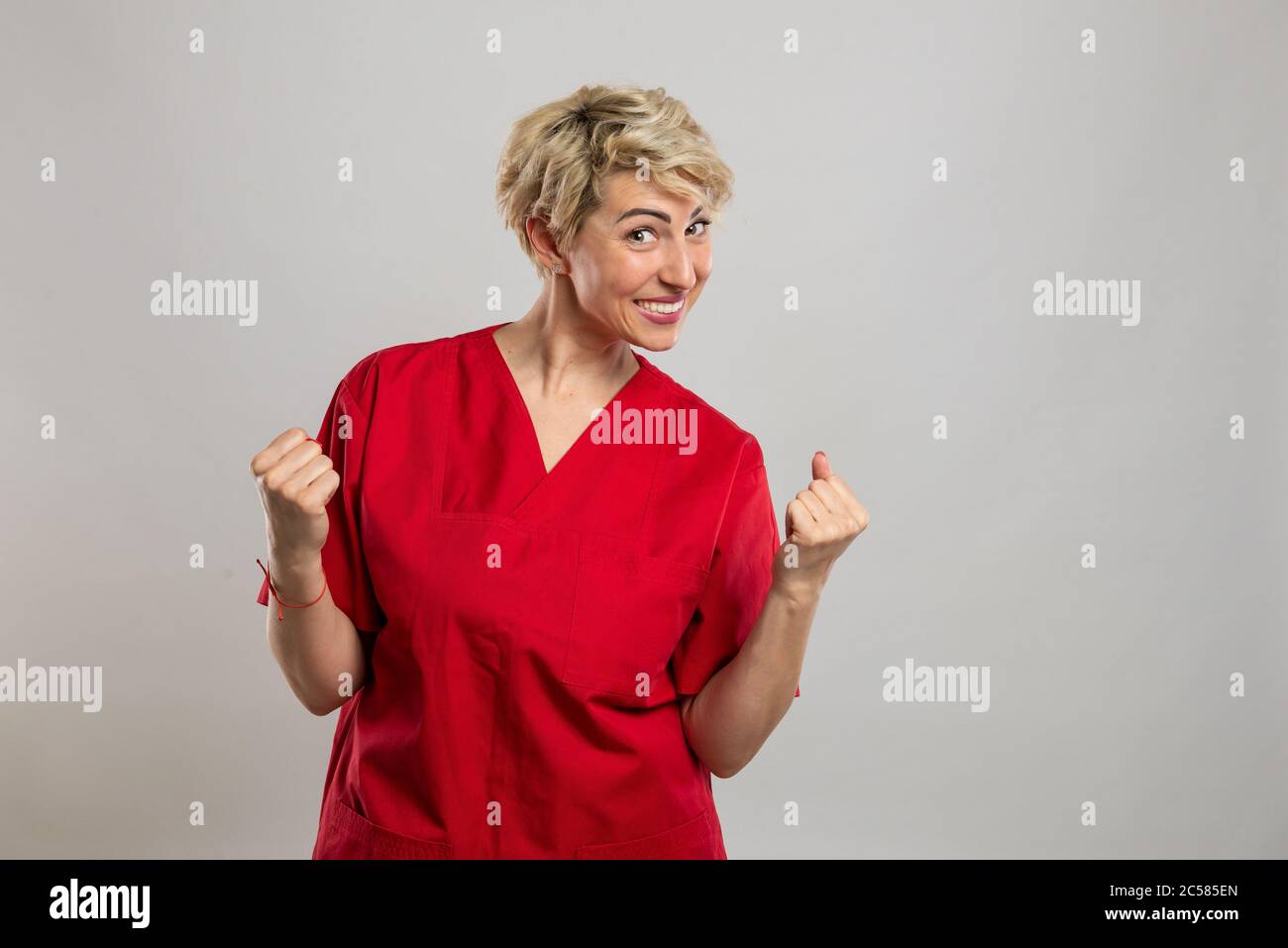 Portrait of young attractive female nurse making winner gesture on grey ...