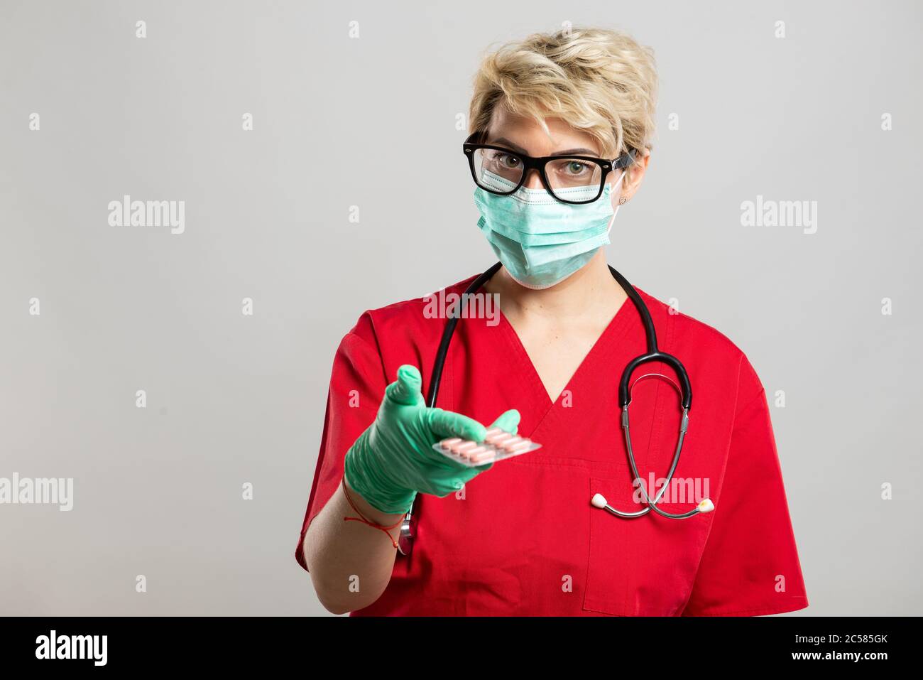Portrait of female doctor wearing face mask handing tablets on grey ...