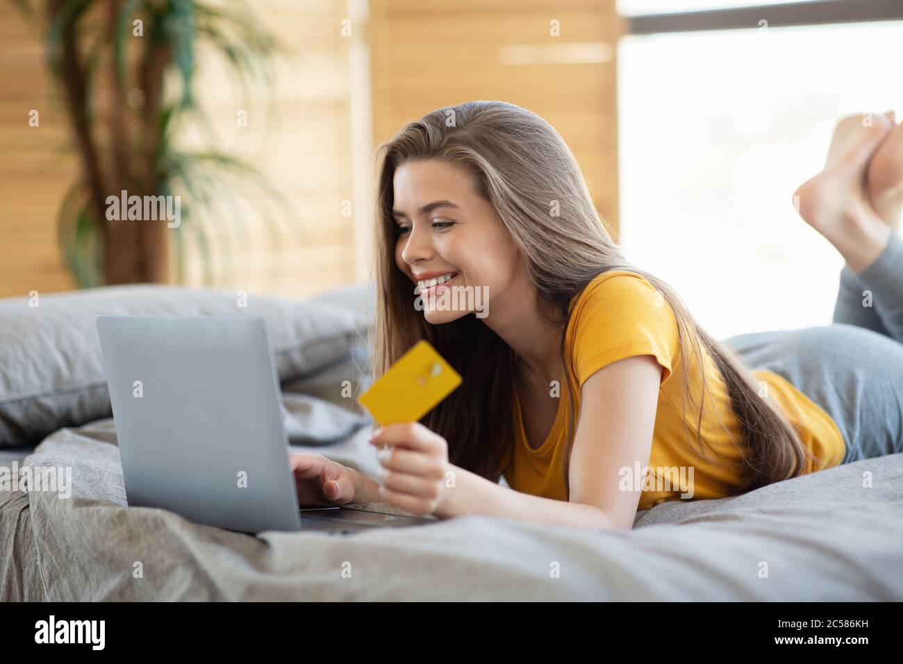 Lovely girl with laptop computer and credit card shopping online on bed ...