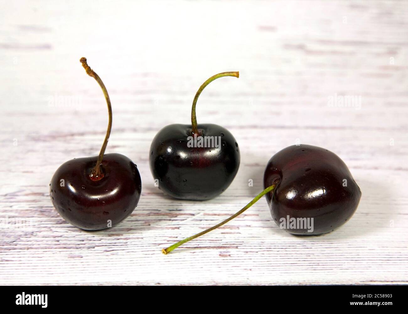 Three juicy and ripe sweet cherries on a light wooden background Stock ...