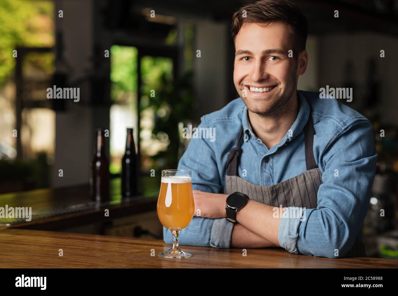 Fresh lager with foam. Smiling barman with crossed arms, behind bar ...