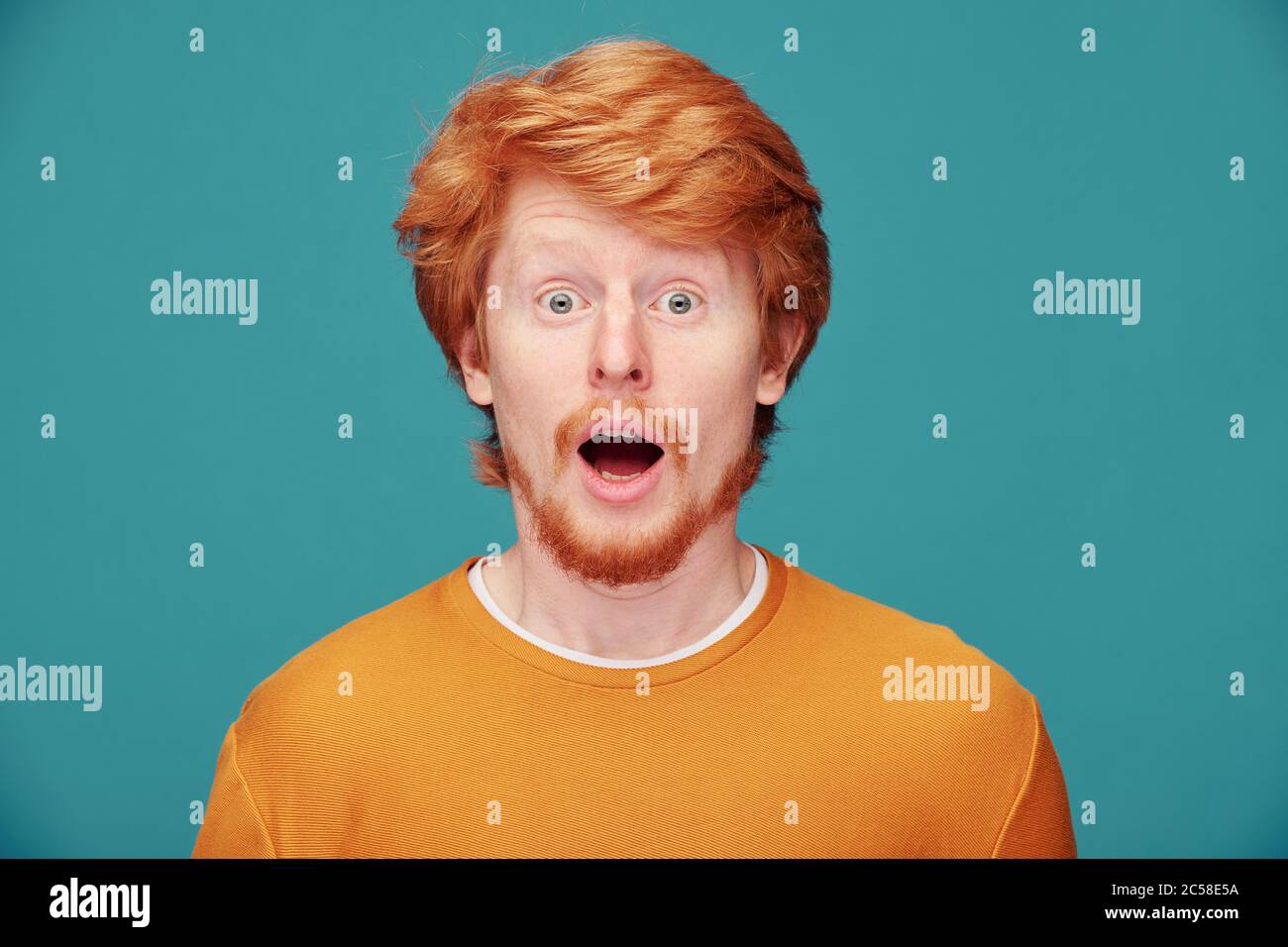 Portrait of emotional young red-bearded man surprised by news keeping ...