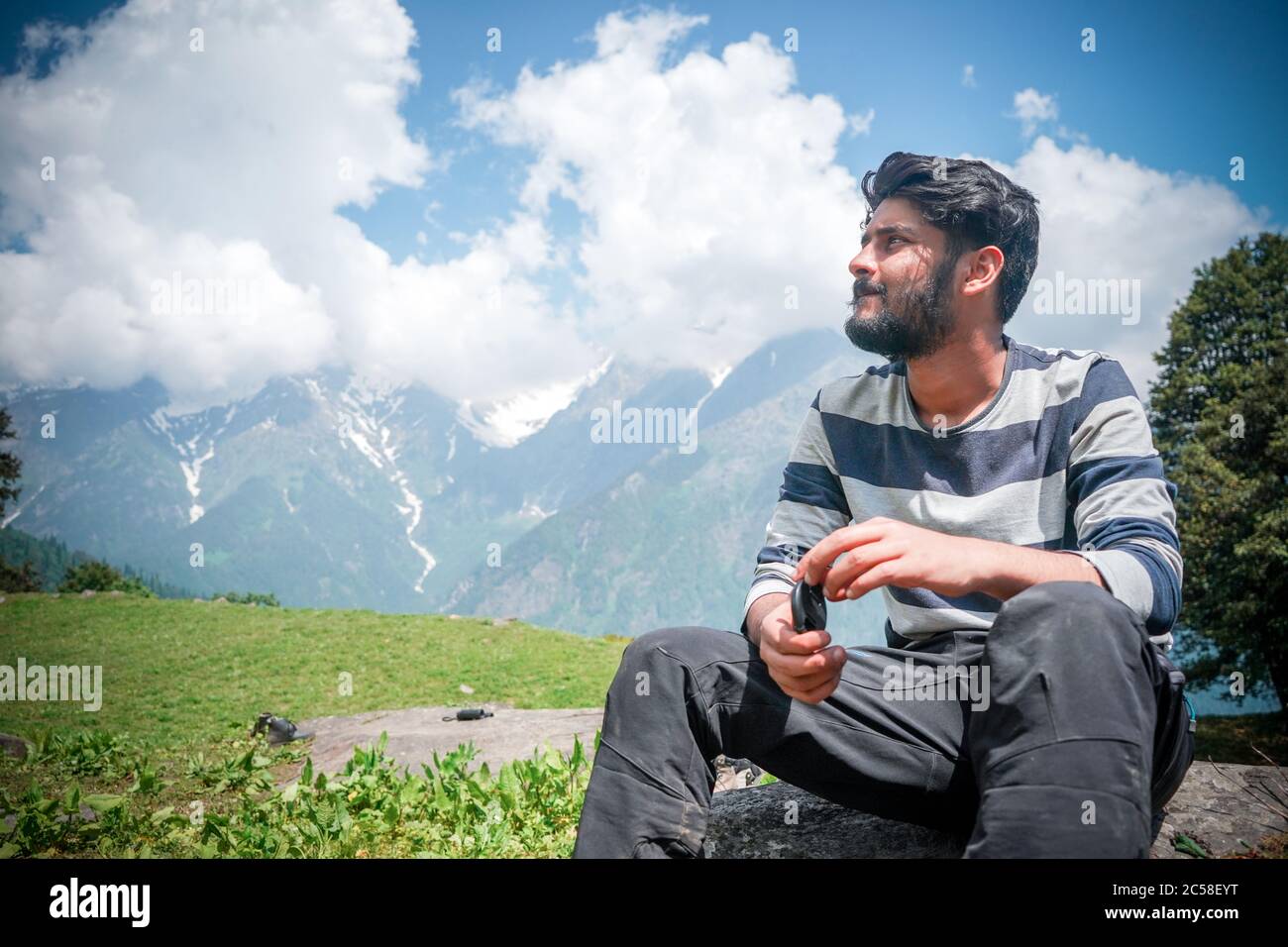 Young Indian man sitting on the rock with the mountains in a background ...