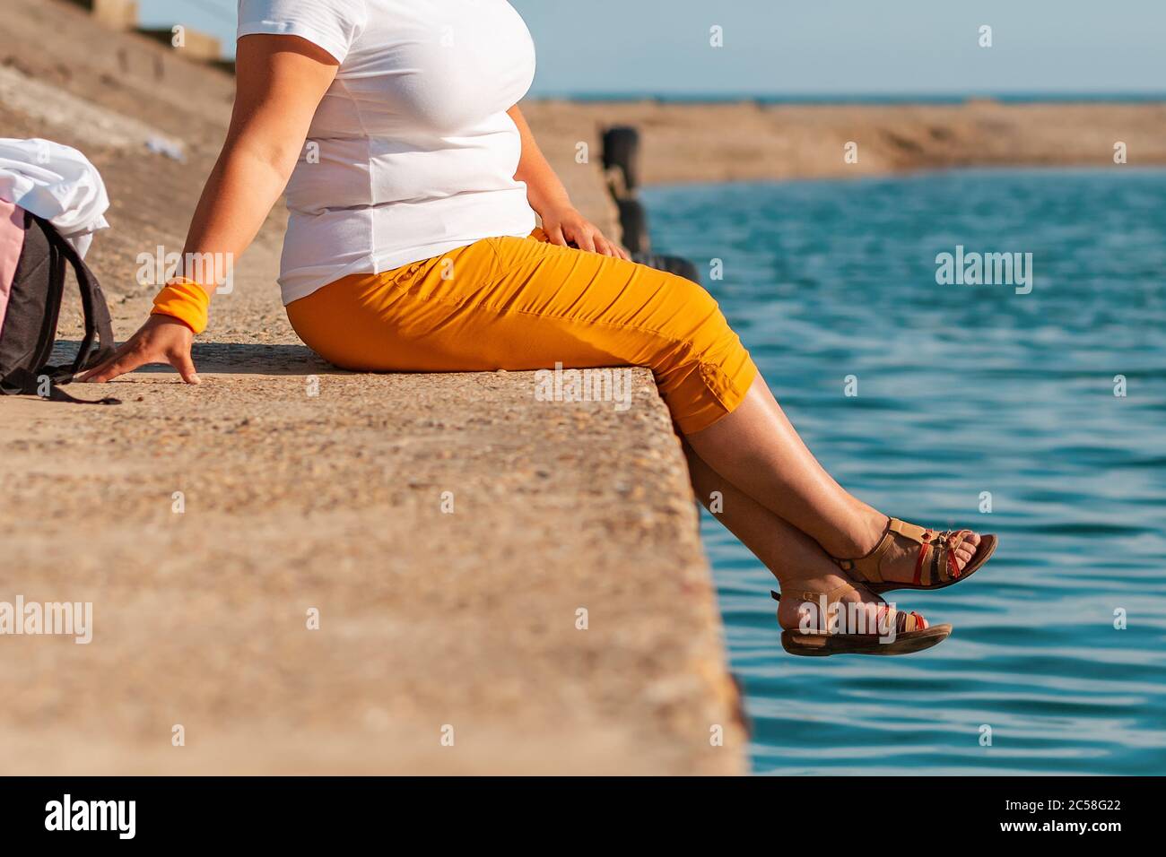 Portrait of an overweight woman poses while sitting on a sea pier. Side ...