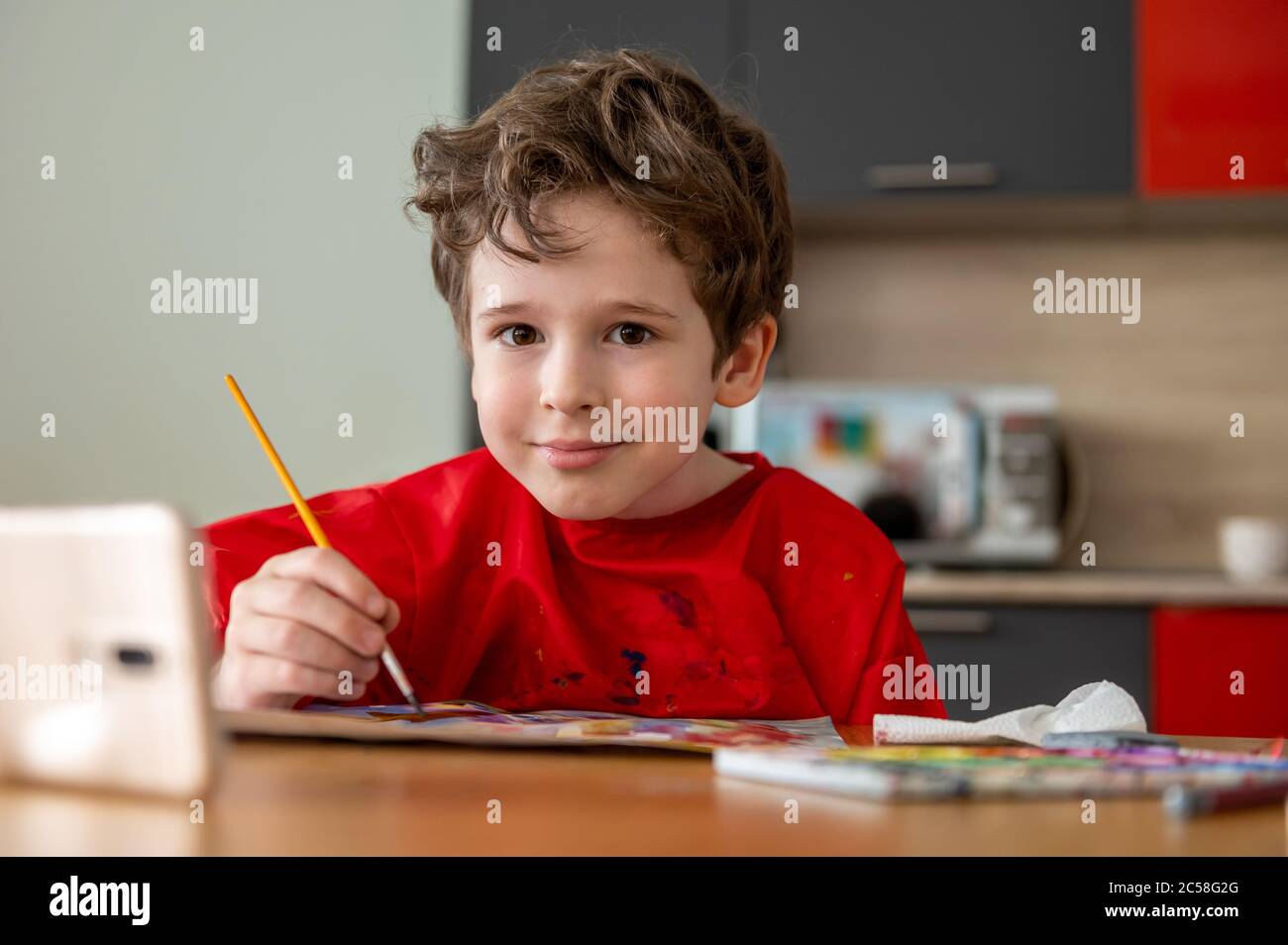 Pretty happy little boy drawing at home using online distance lessons ...