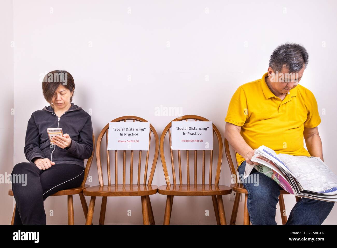 People seated in-between two chairs at public place, with Social ...