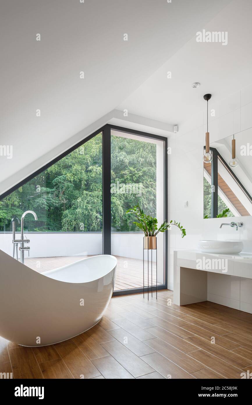 Elegant attic bathroom with big bathtub, wooden floor and balcony ...