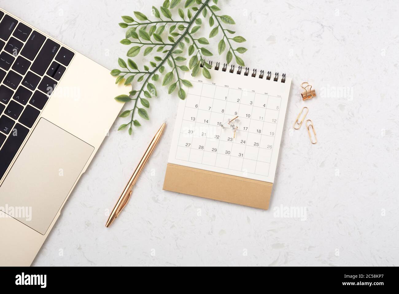 Calendar with gold pen and green leaf on white quartz table, top view ...