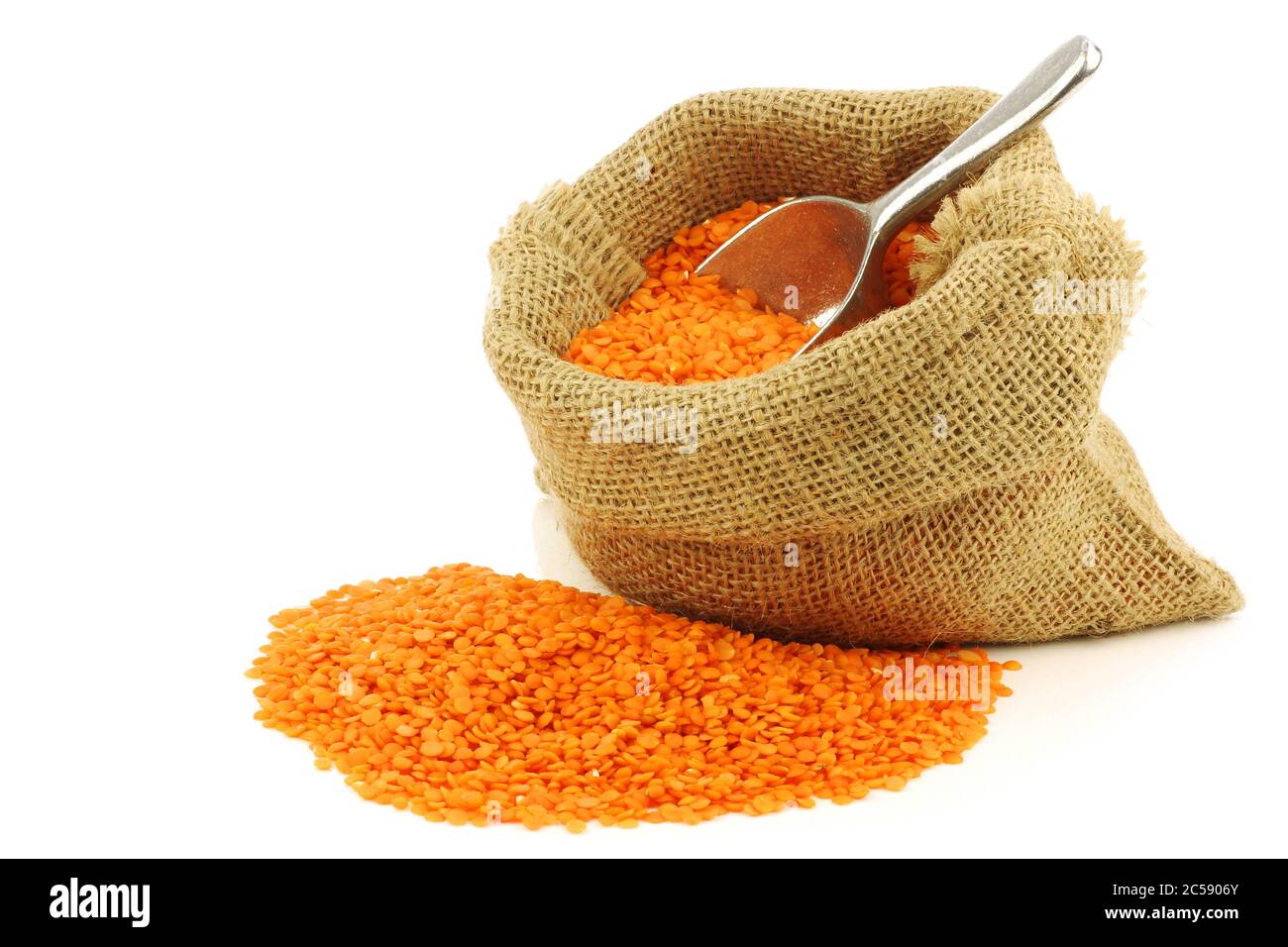red lentils in a burlap bag with a metal scoop on a white background ...