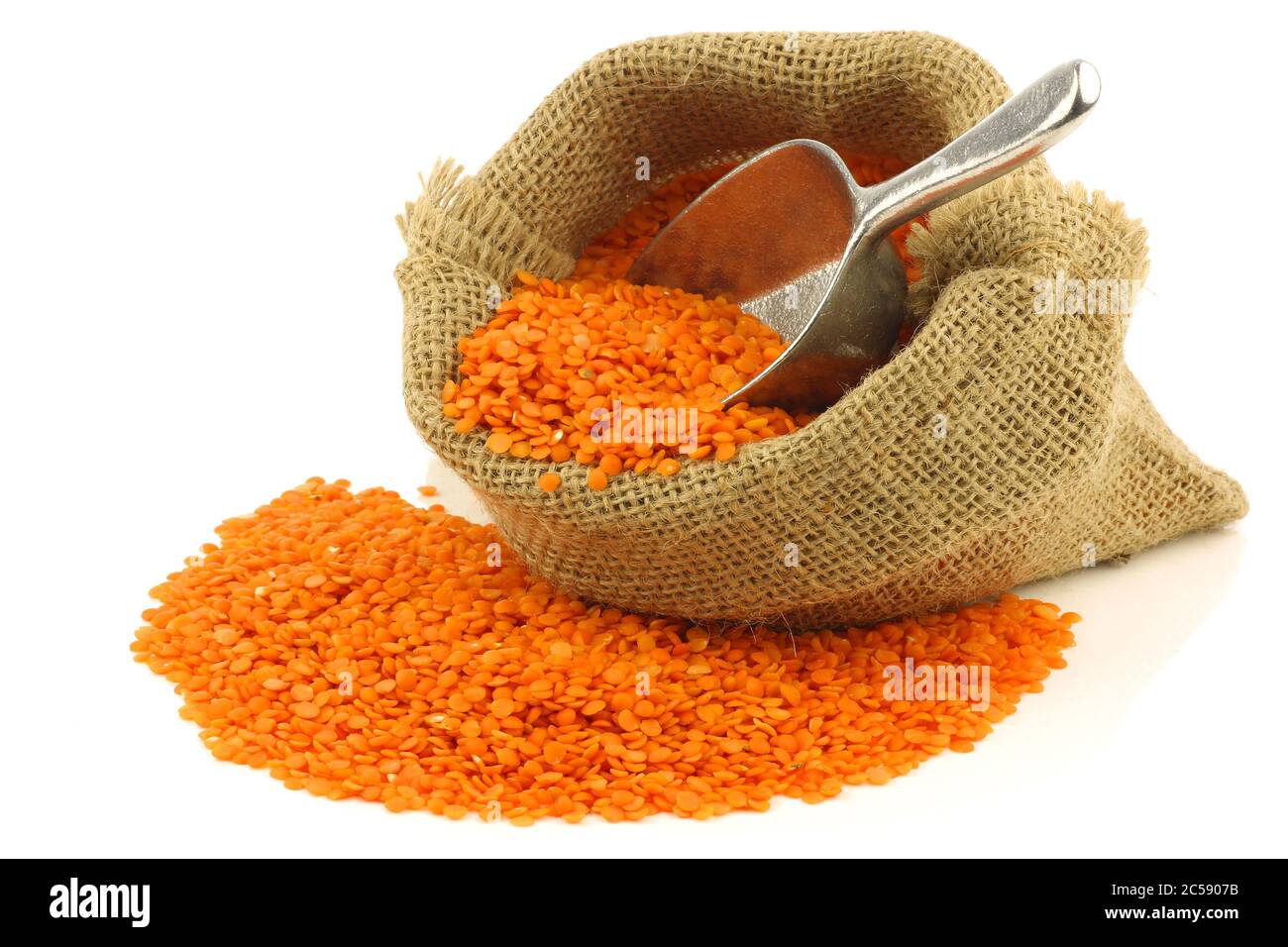 red lentils in a burlap bag with a metal scoop on a white background ...