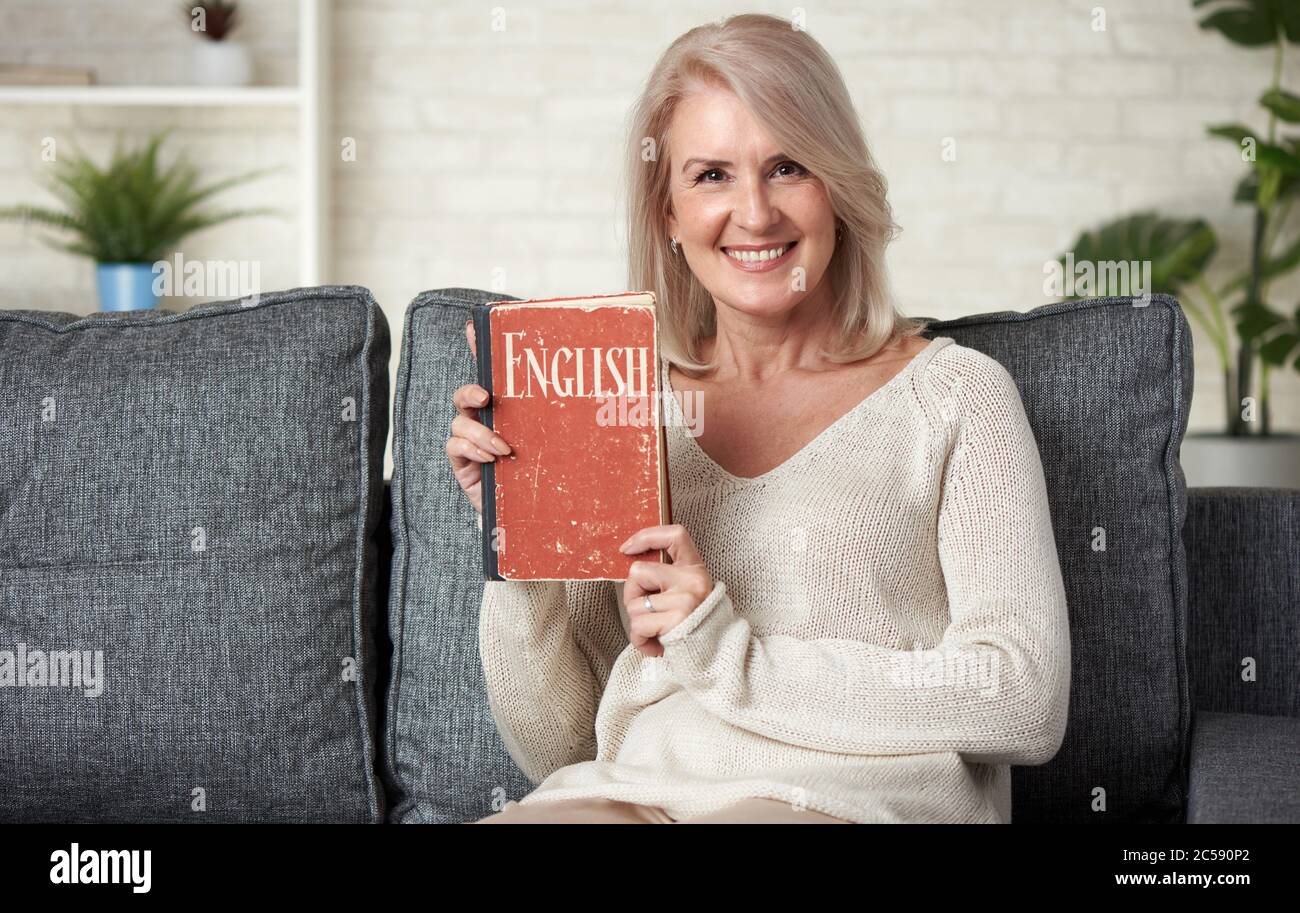 Beautiful 50 years old woman relaxing on sofa at home. Reading an ...