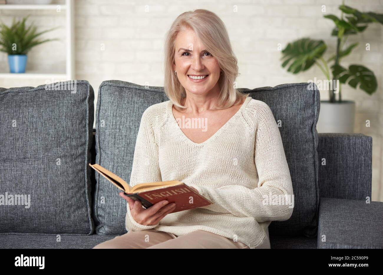 Beautiful 50 years old woman relaxing on sofa at home. Reading an ...