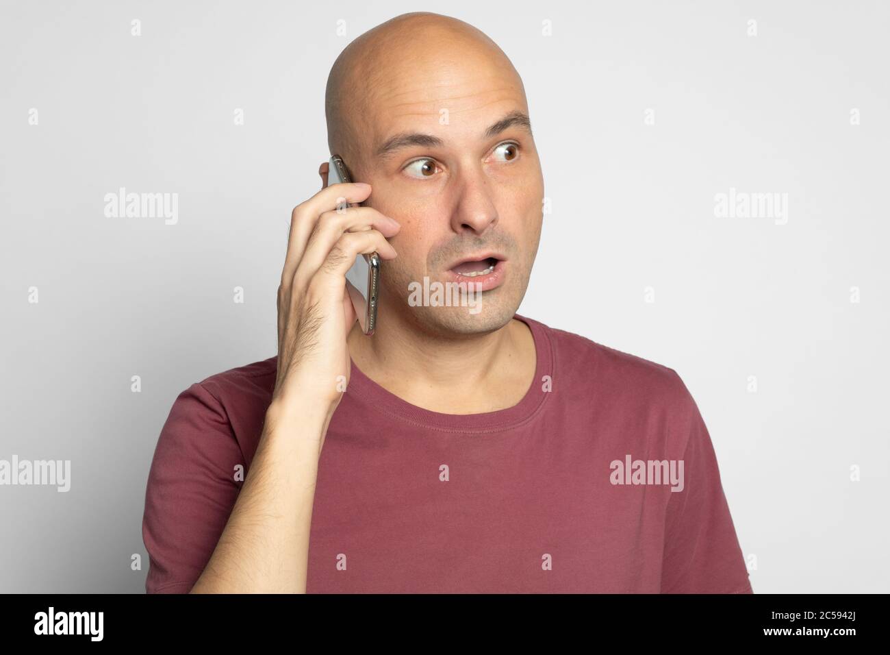 Caucasian middle aged bald man talking on phone with an surprised ...