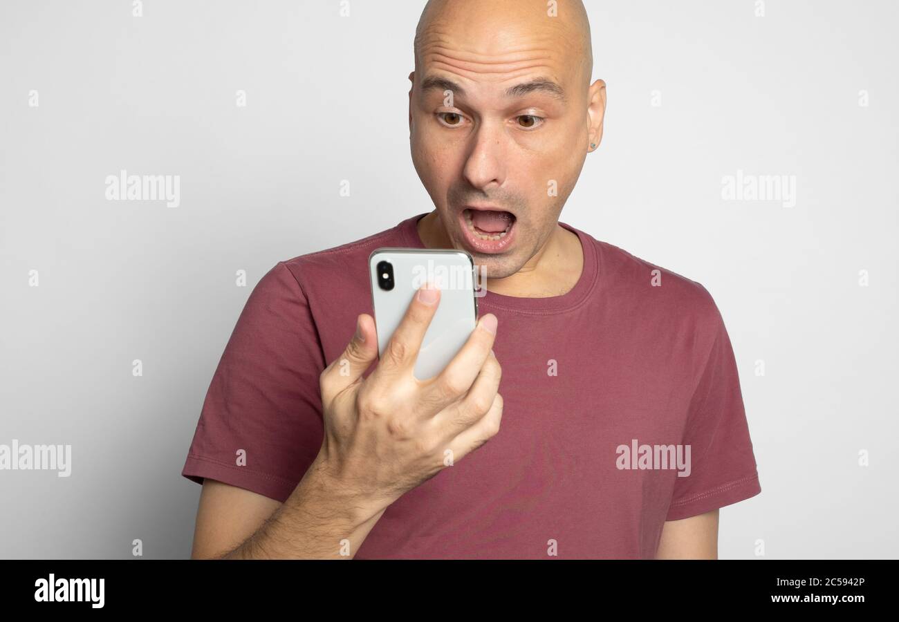 Shocked man looking at his smartphone over grey studio wall Stock Photo ...