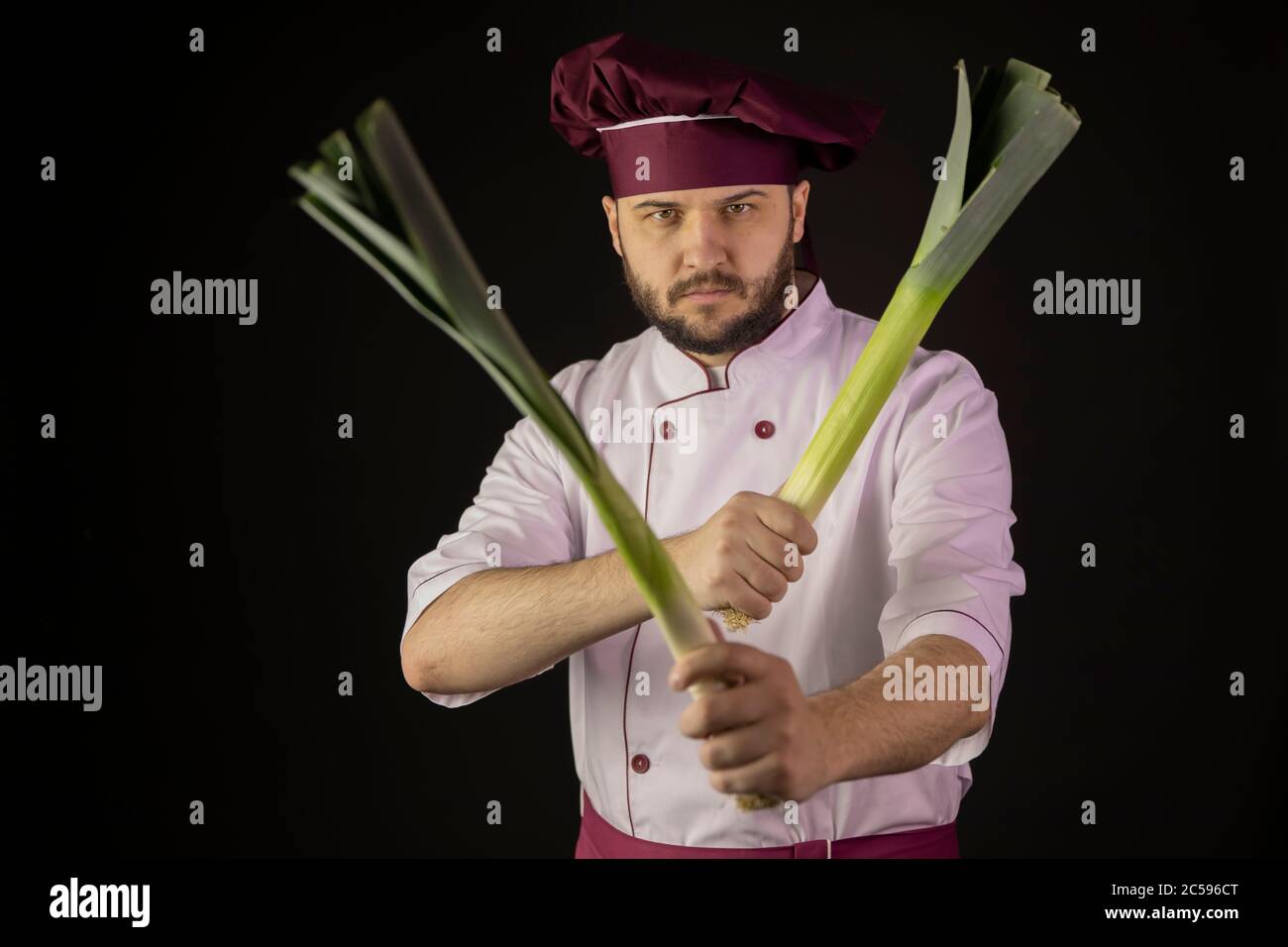 Chef man in uniform holds two leek stalks crossing them like weapon ...