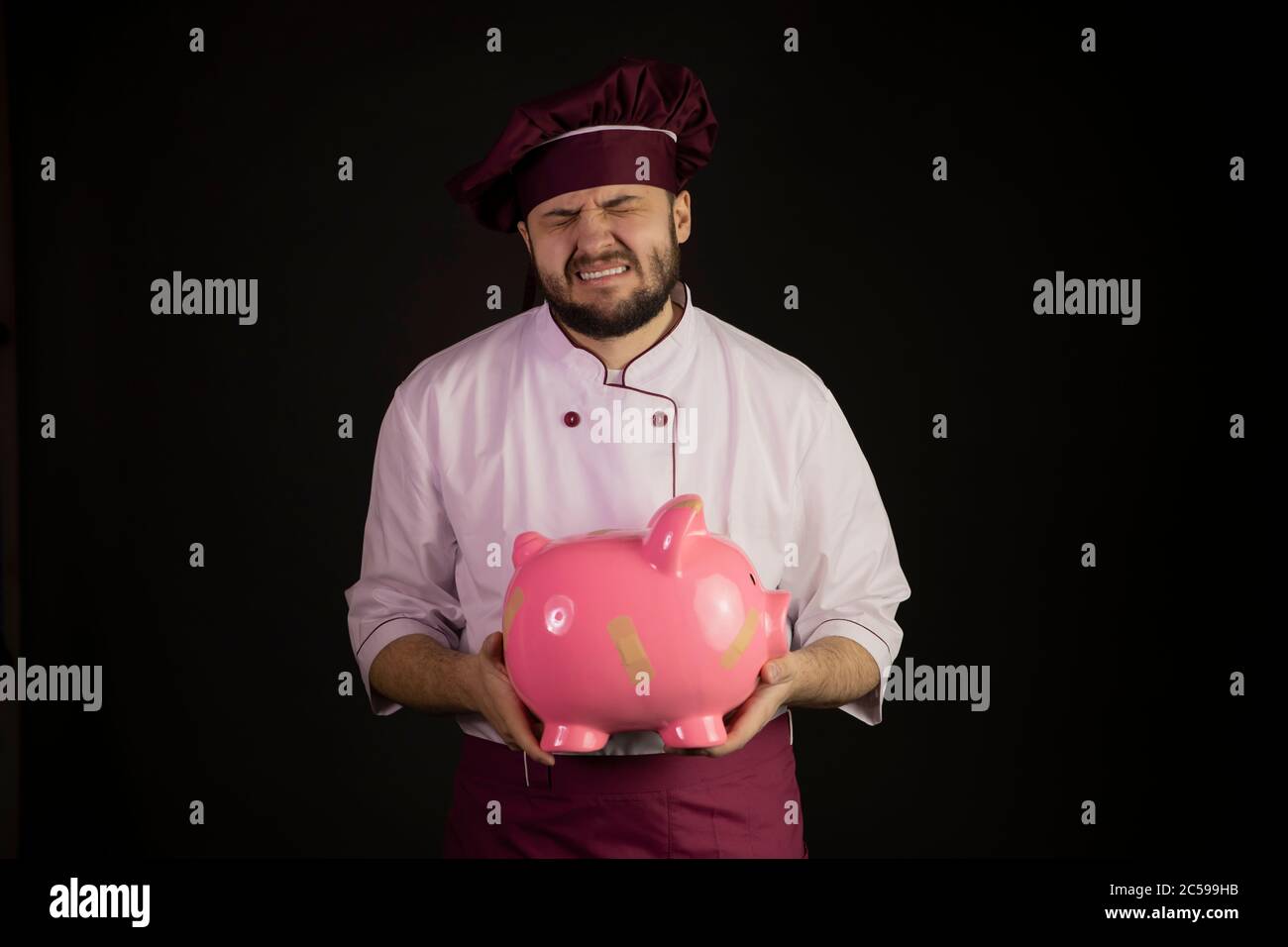 Crying chef man in uniform holds broken pink piggy bank on black ...