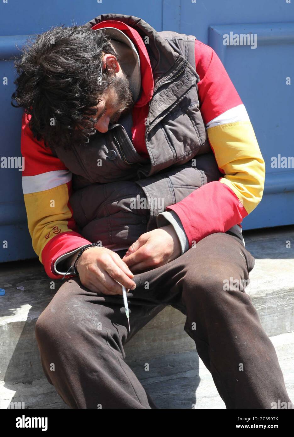 A drug addict with a needle still in his hand on the streets of Athens ...