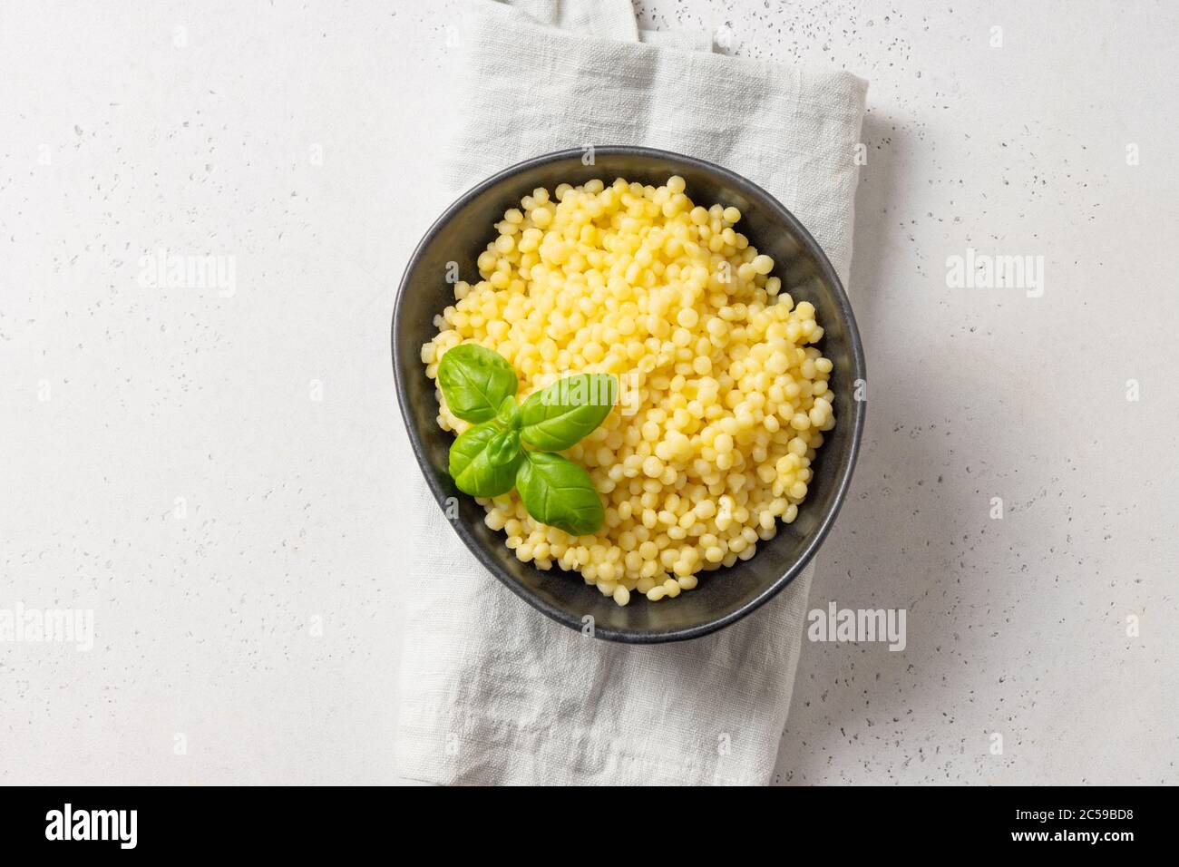 Pasta ptitim decorated basil leaves in black bowl on white. Top view ...