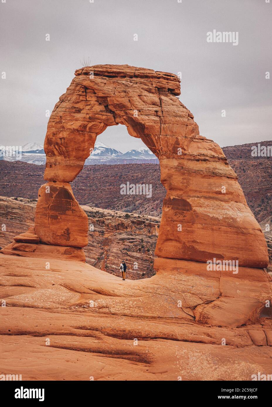 A man with a child is standing under Delicate arch at Arches NP Stock ...