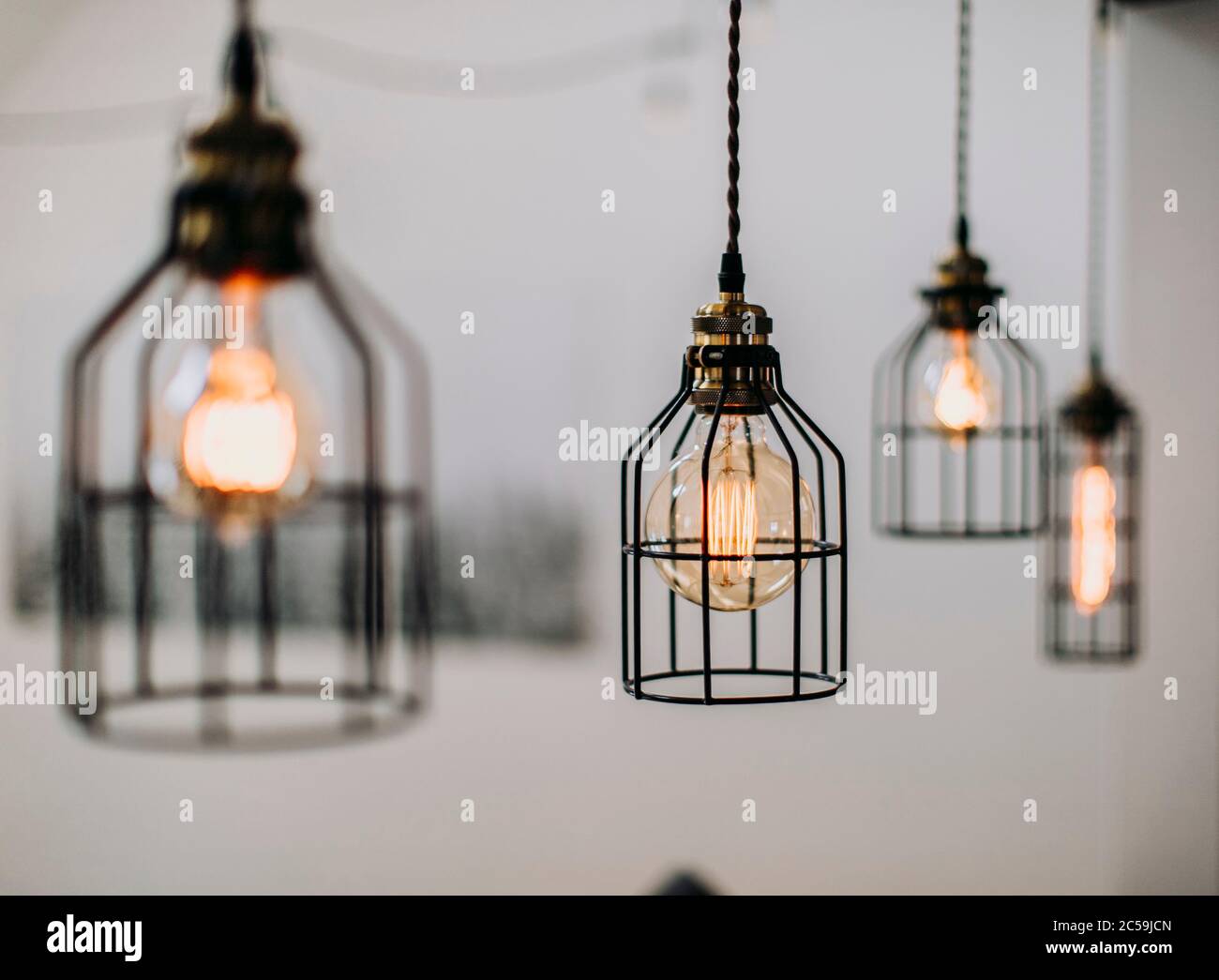 lightbulbs protected by wire hang in front of a white wall inside Stock ...
