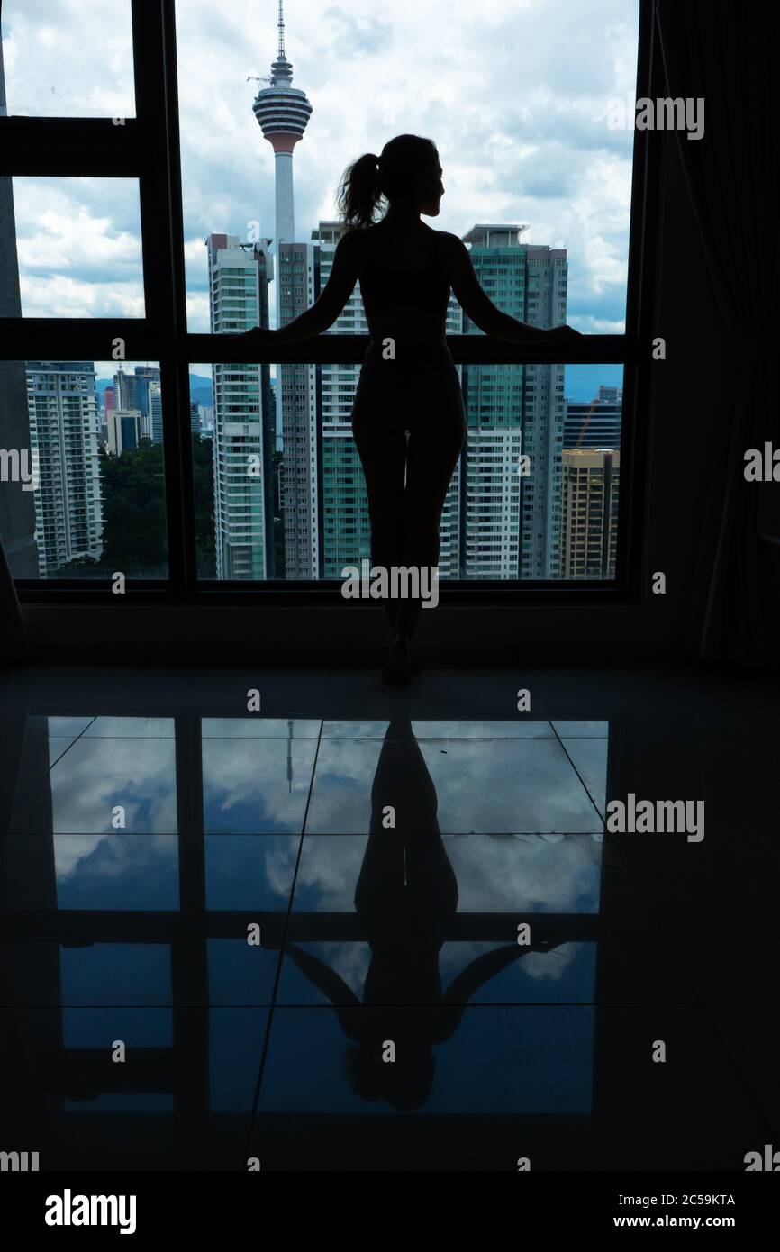 A slender girl is looking at the city through a large window. High ...