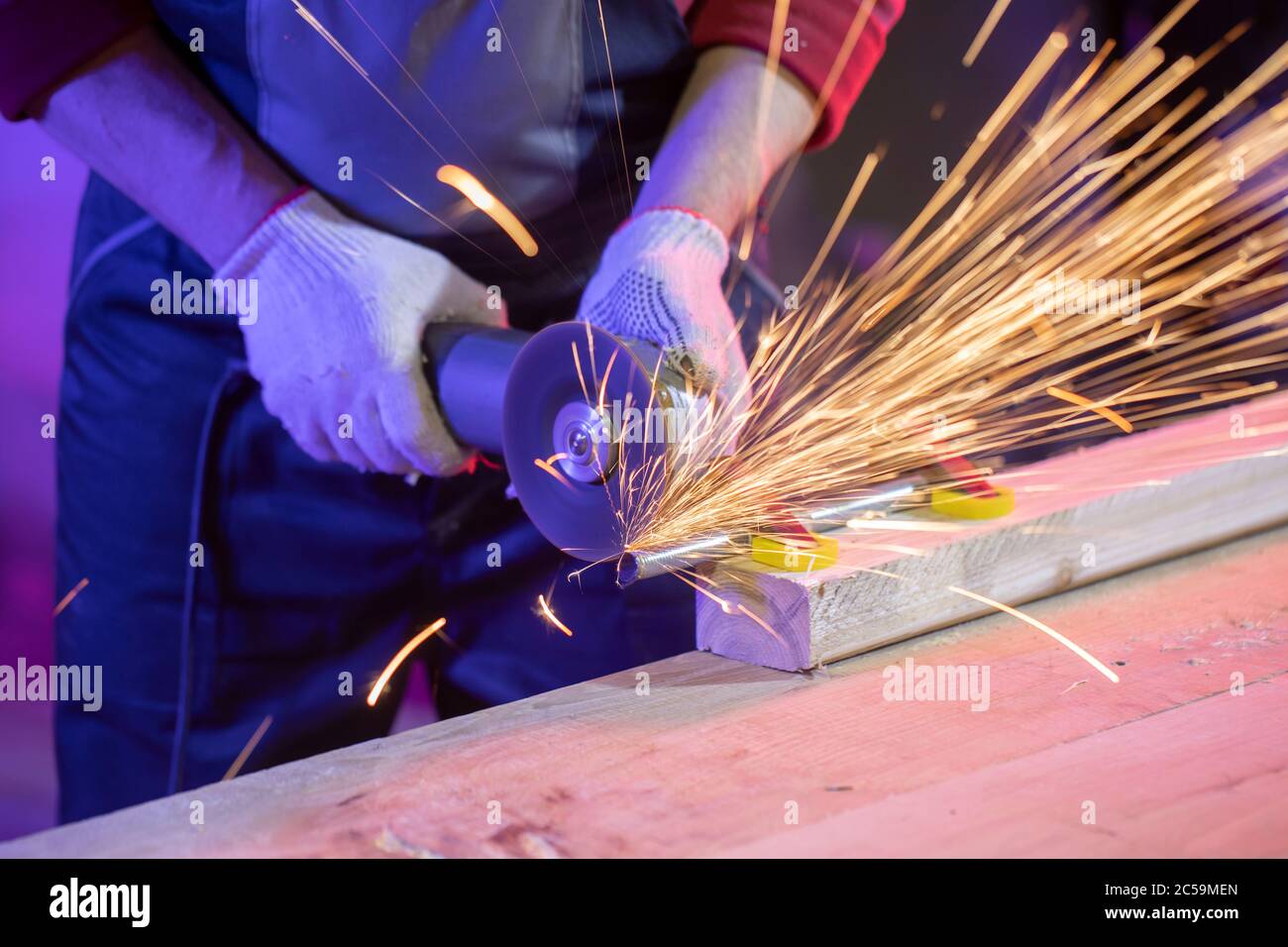 close-up of men's hand grinding metallic tube with sparks in coloured ...