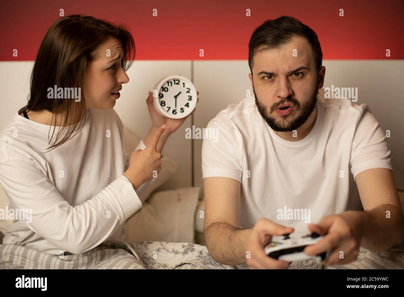 Male gamer with joysticks plays video game in bed at night, girl can't ...