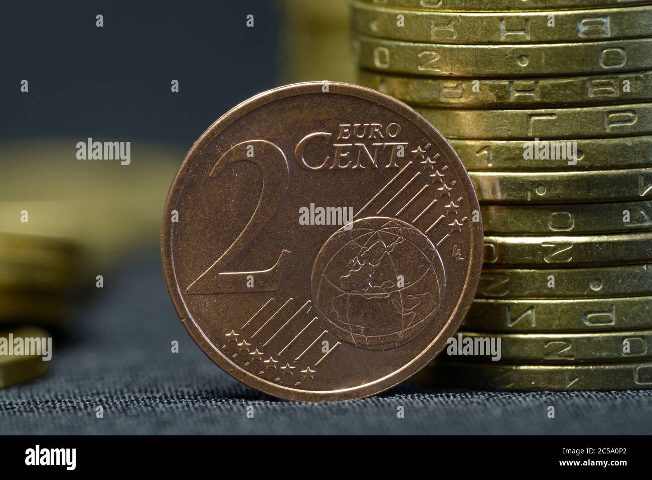 An old, 2009 year, two euro cent coin put on the edge in front of piles ...
