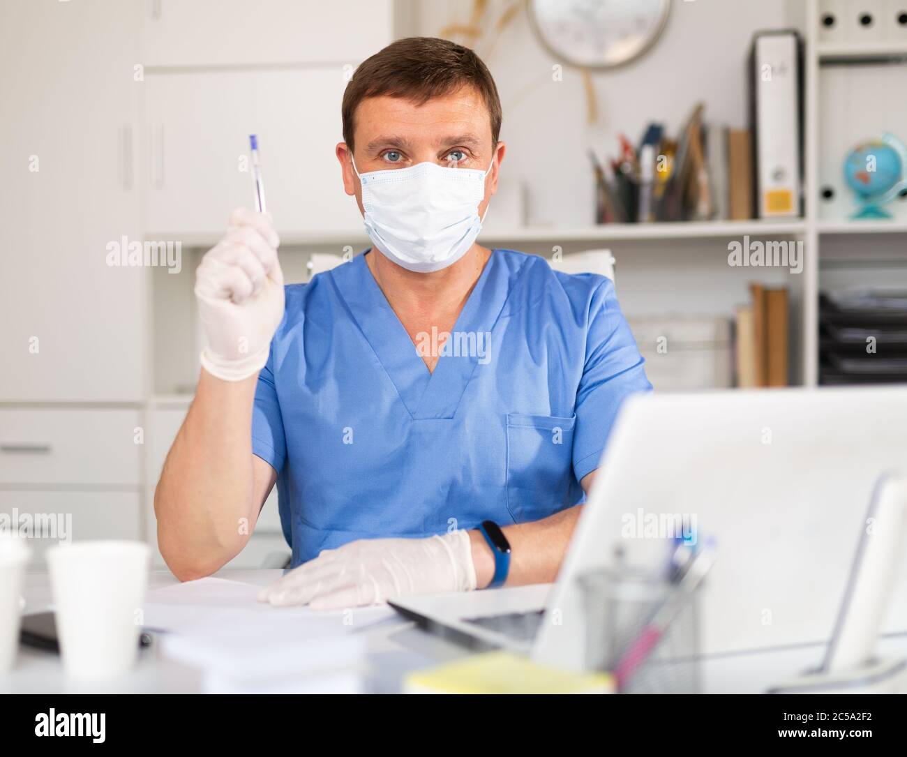 Portrait of male doctor in face mask and gloves working on laptop ...